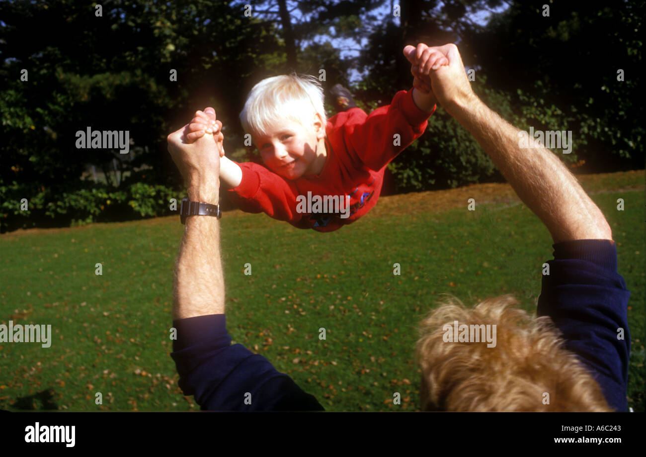 Young boy being spun around in the air by arms by father in the park ...