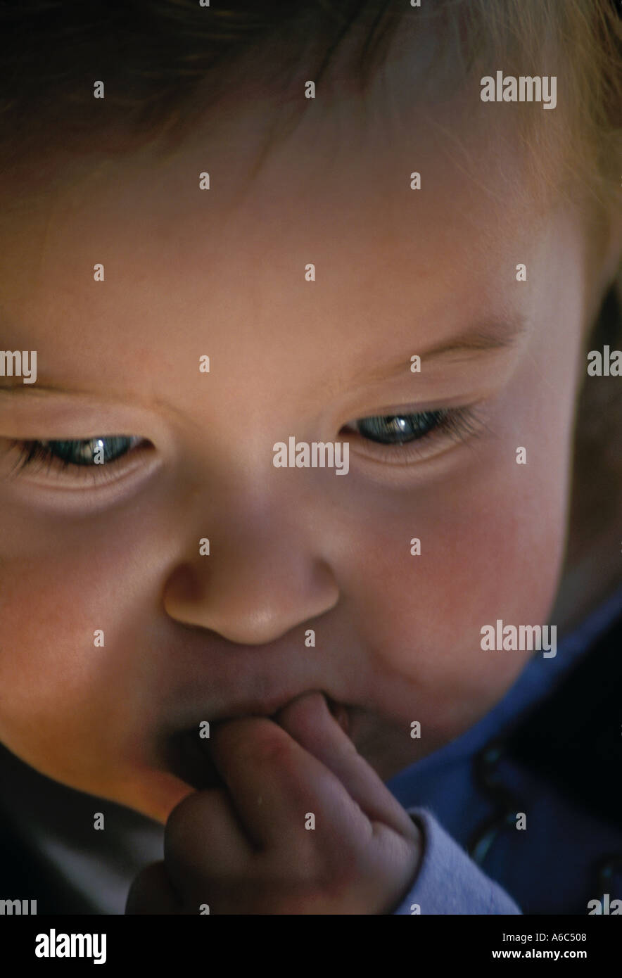 Face of one white Female toddler with hand to mouth looking down ...