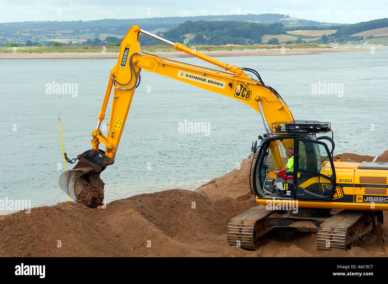 Large bright yellow JCB digger on the beach at Exmouth Devon renewing ...