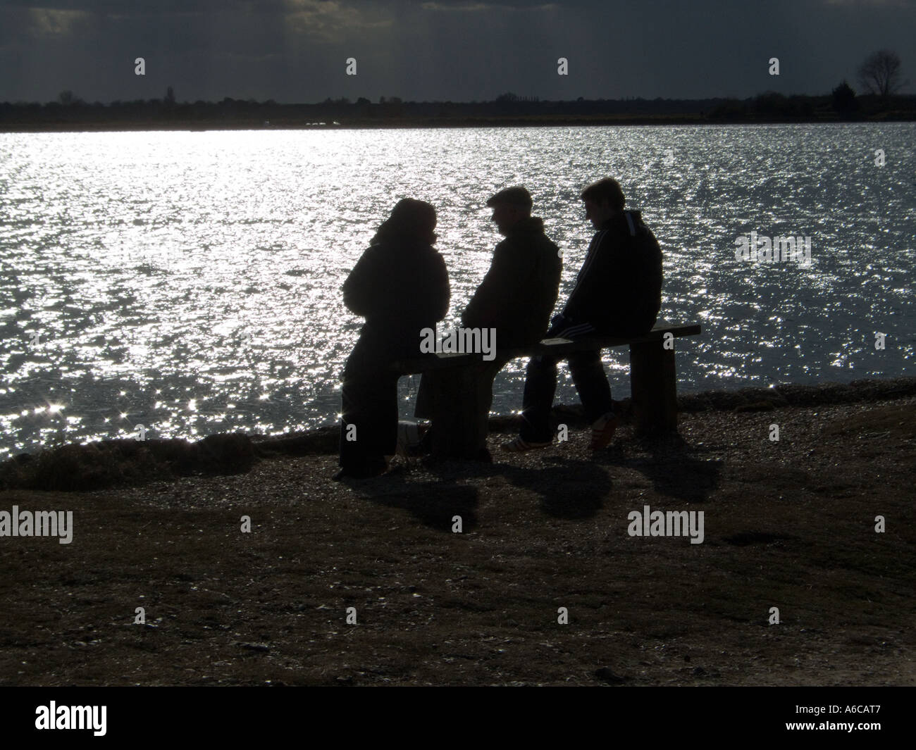 people sitting on a bench in the sun by water Stock Photo - Alamy