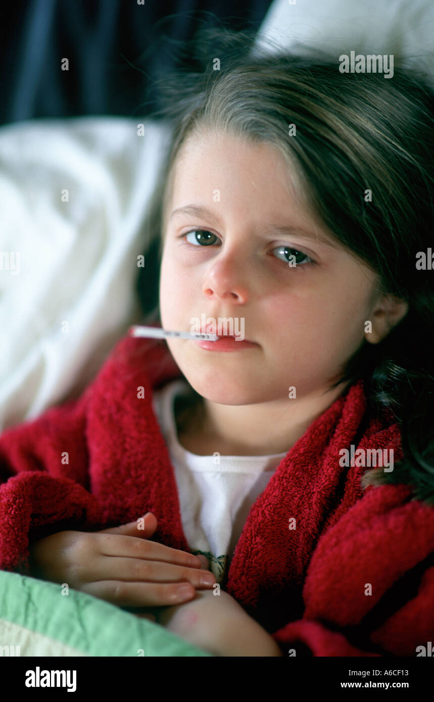 child laying in bed looking sick and feverish with thermometer in her ...