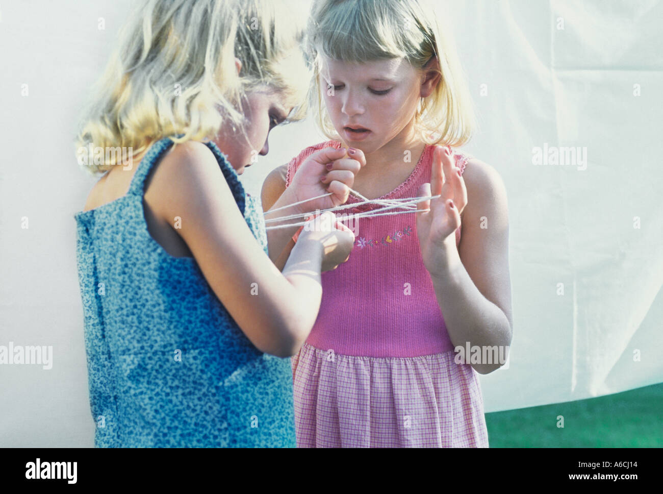 Two young girls in dresses playing string game in front of sheets ...