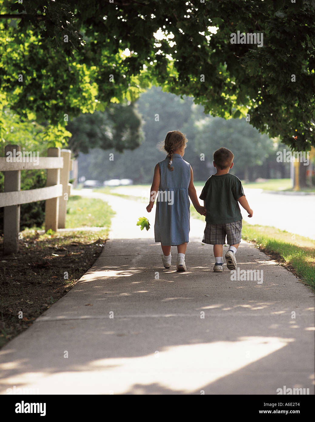Brother and Sister (2 and 5 years) walking hand in hand down sidewalk ...