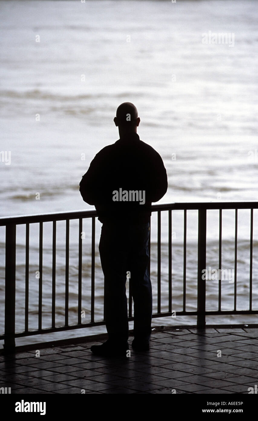 Young man standing alone looking out over the fast flowing river Rhine ...