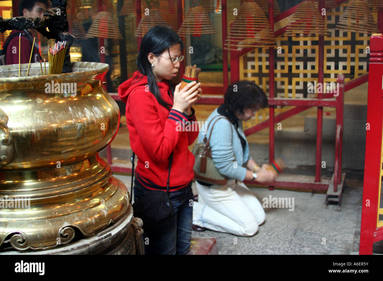 Chinese woman shaking fortune sticks in a bamboo cup; one kneeling in ...