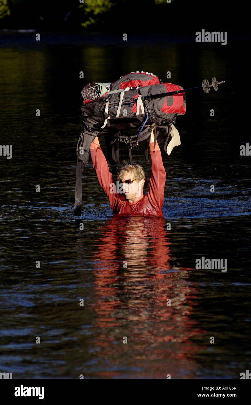 A man carrying a backpack over his head while crossing a river Stock ...