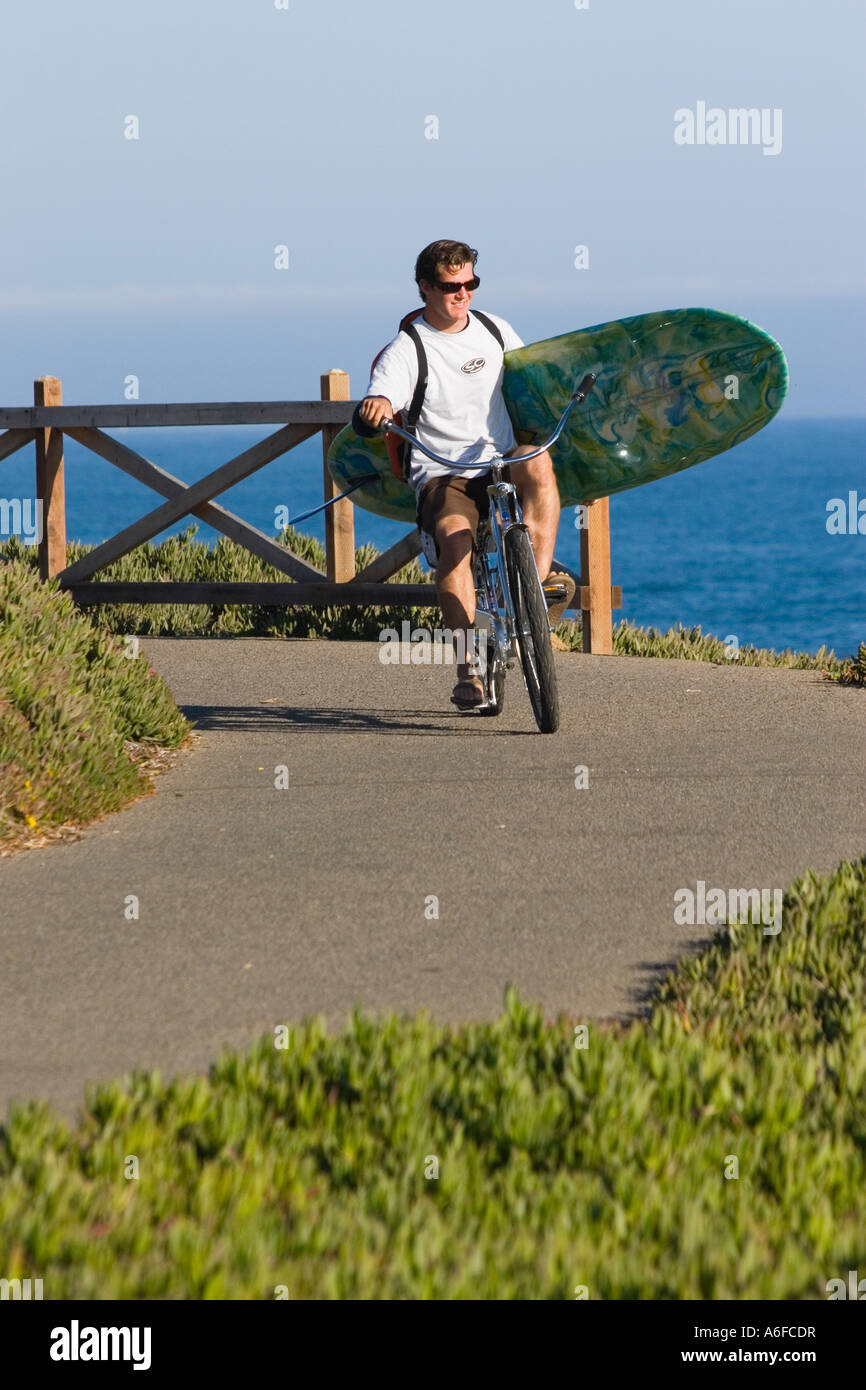 A man riding a bike with a surfboard above the ocean in Santa Cruz ...