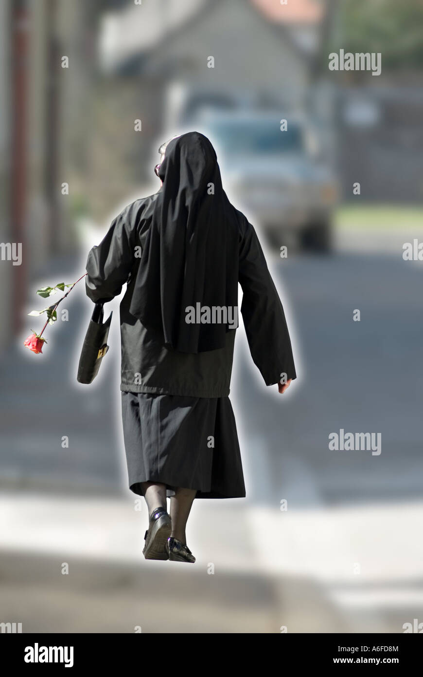 nun in black with a red rose walking on a sidewalk in the city of ...