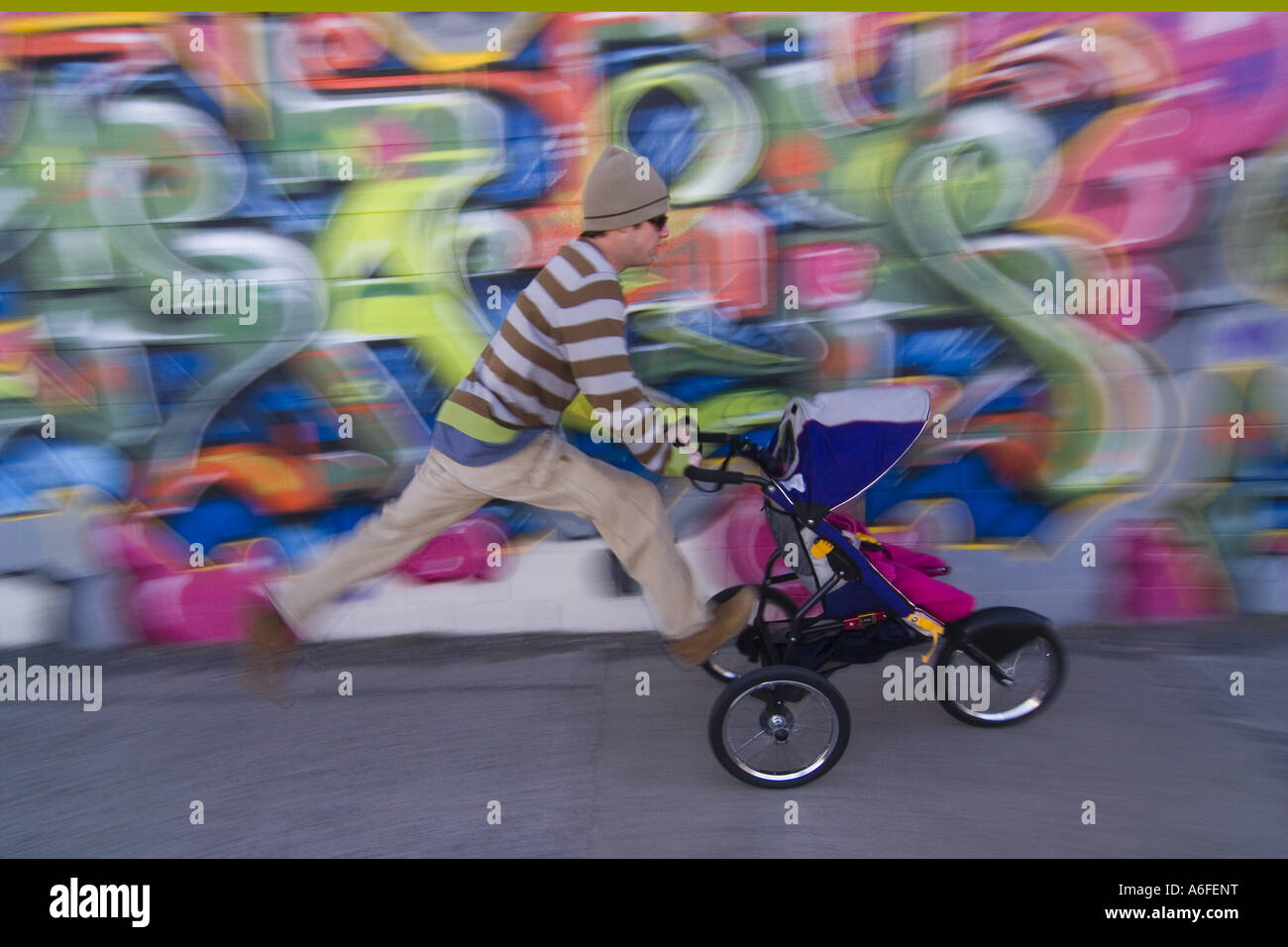 A man pushing a child in a baby stroller past a wall of graffiti in ...