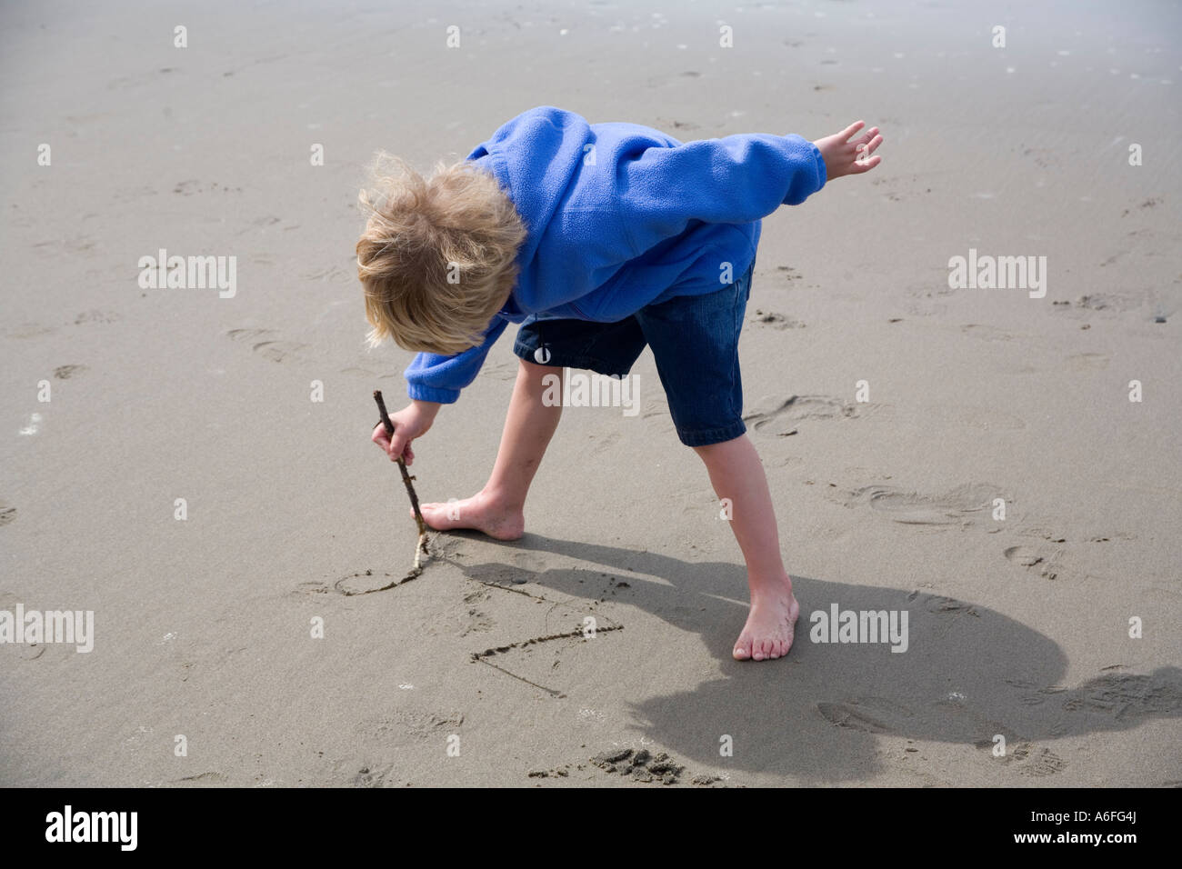 Boy writing in the sand with a short stick Stock Photo - Alamy