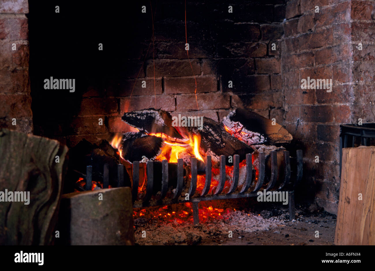 Log fire burning indoors in a metal grate with brick wall Warming in ...