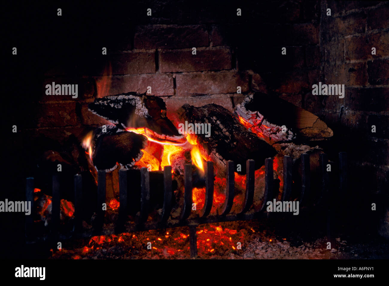 Log fire burning indoors in a metal grate with brick wall Warming in ...