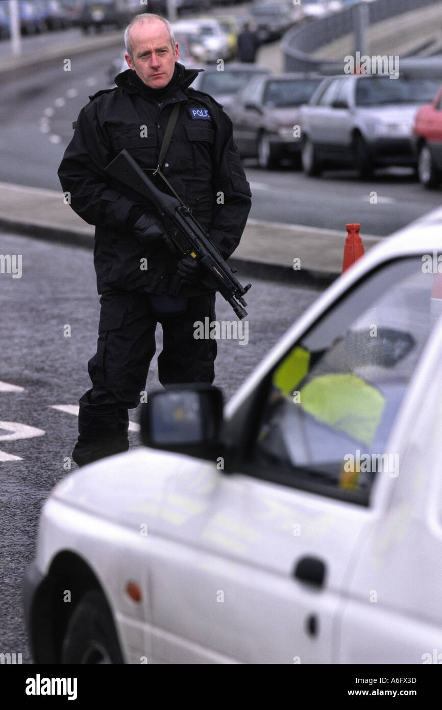 An armed police officer with his automatic weapon at the ready stands ...