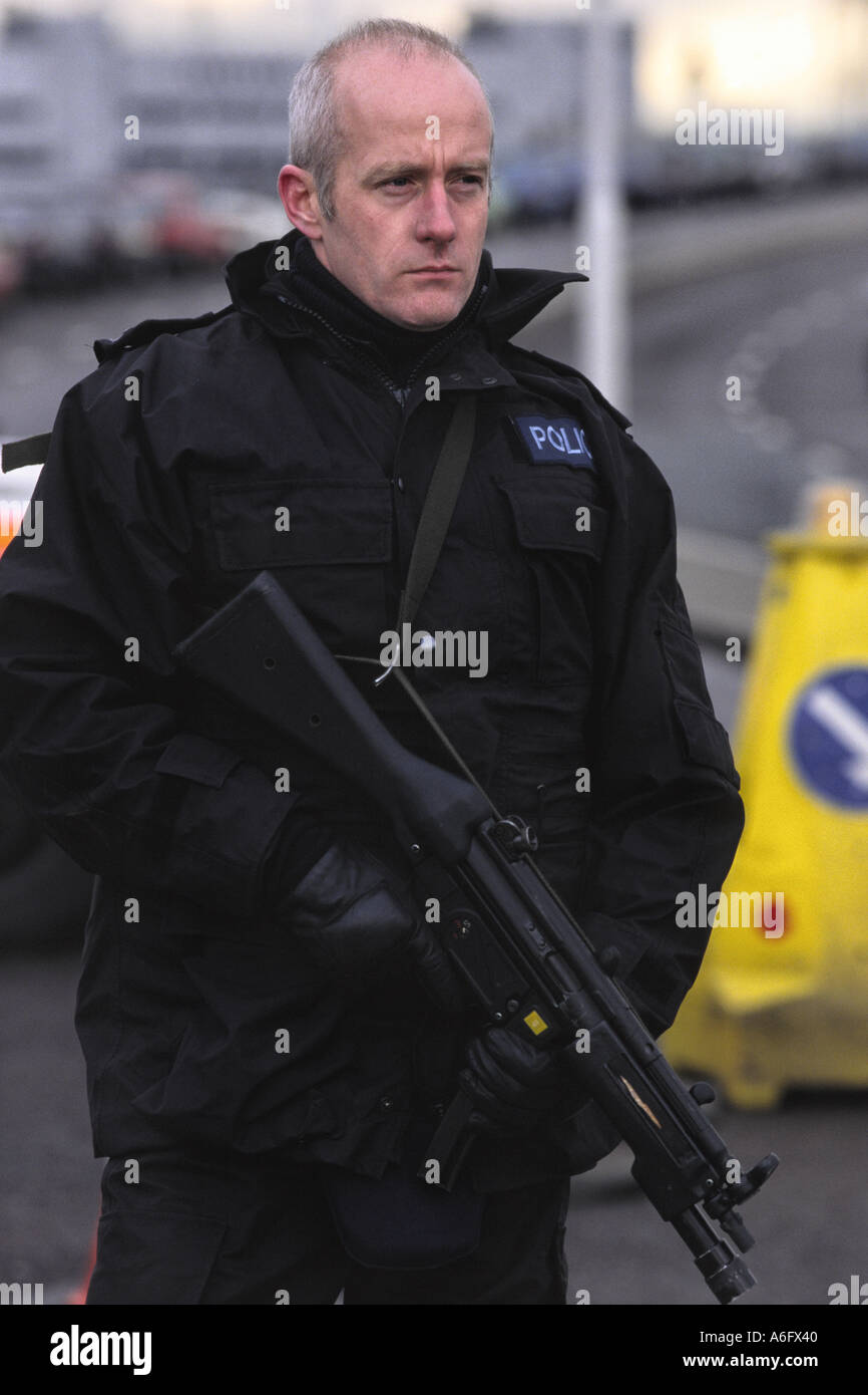An armed police officer with his automatic weapon at the ready stands ...