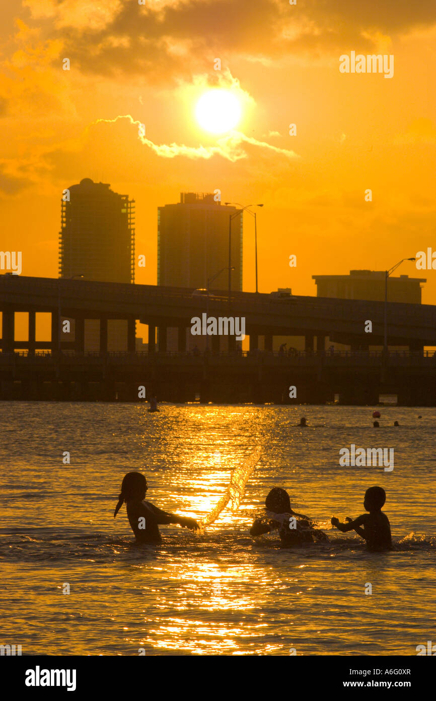 MIAMI FLORIDA USA Swimmers play in shallow water as sun sets over ...