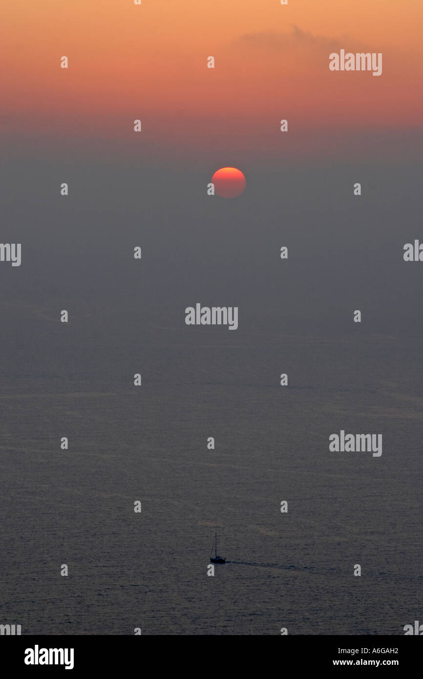 Sunset with sun setting in to the sea and small boat from Greek Island ...