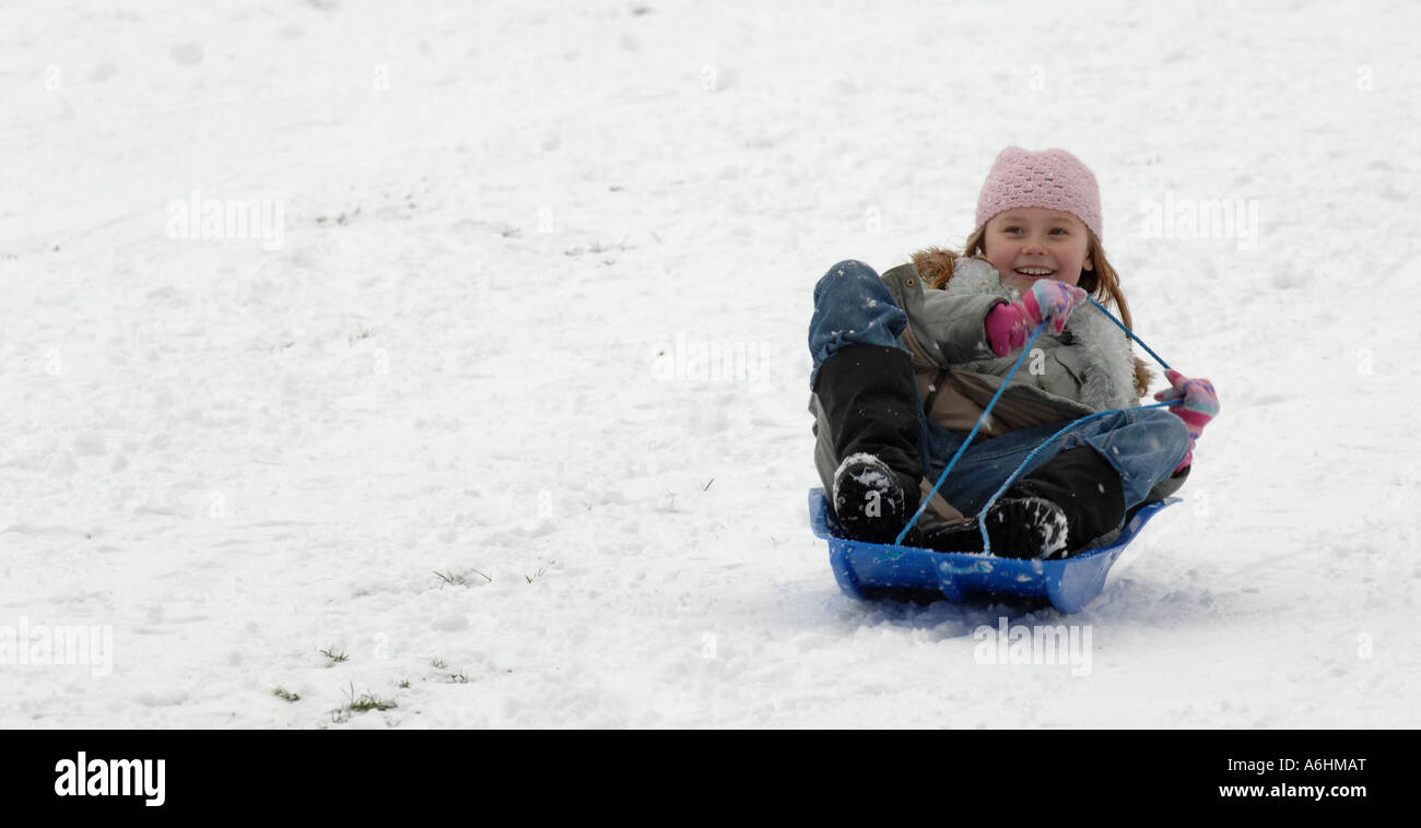 A girl enjoys sledging in the winter snow in England on a blue sledge ...