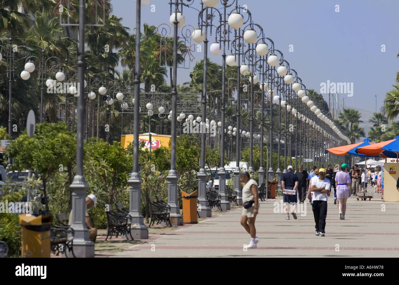 Cyprus visitors walk along Larnaca palm and light lined sea front ...