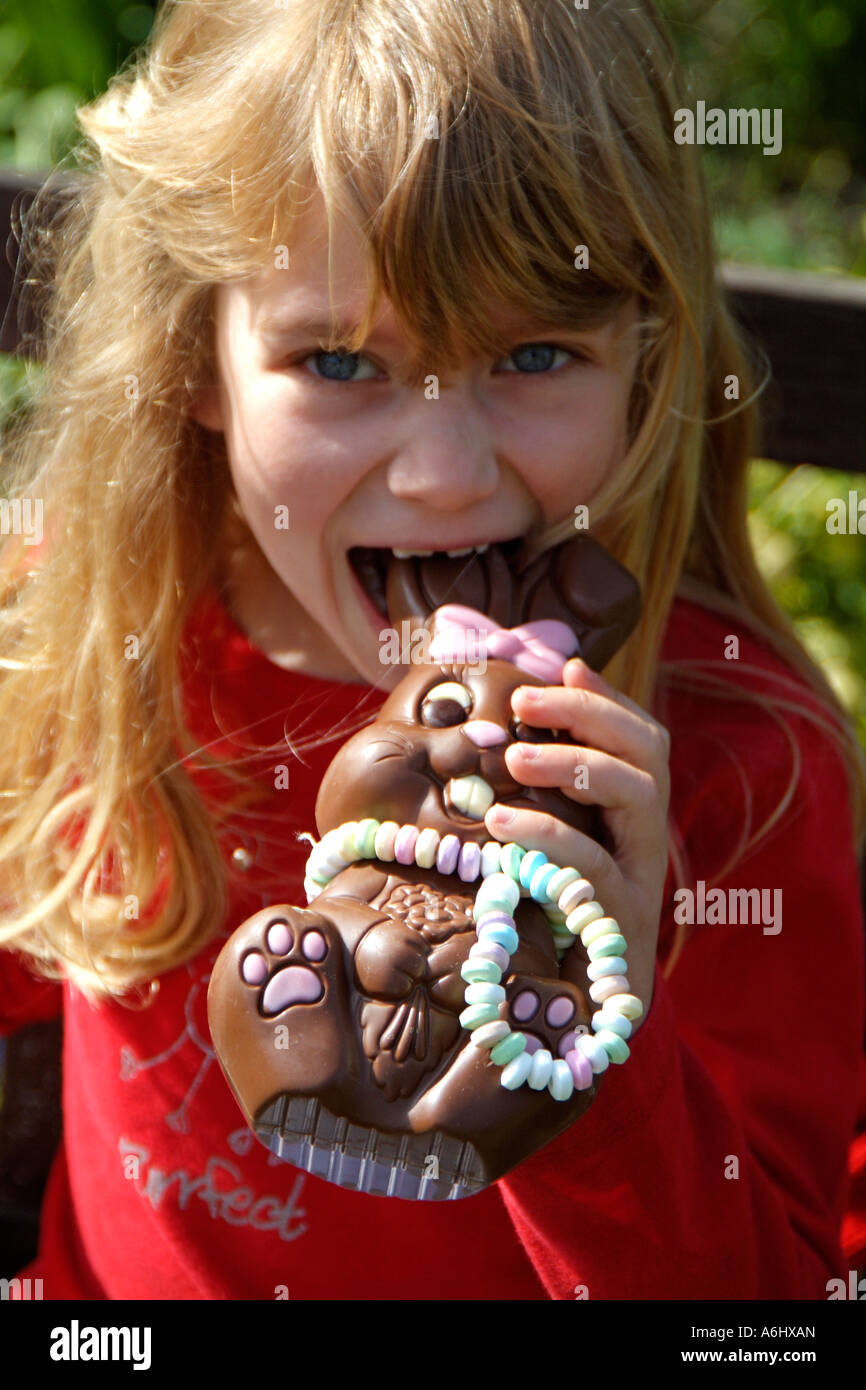 Girl eating a chocolate bunny rabbit which has a necklace of sweets ...