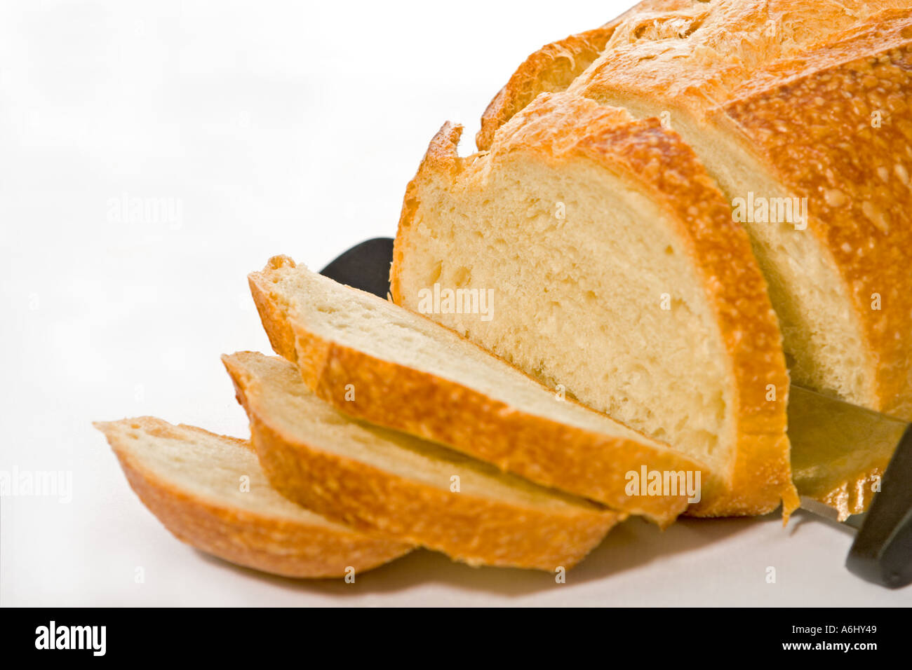Loaf of bread partially sliced with knife on bright white background ...