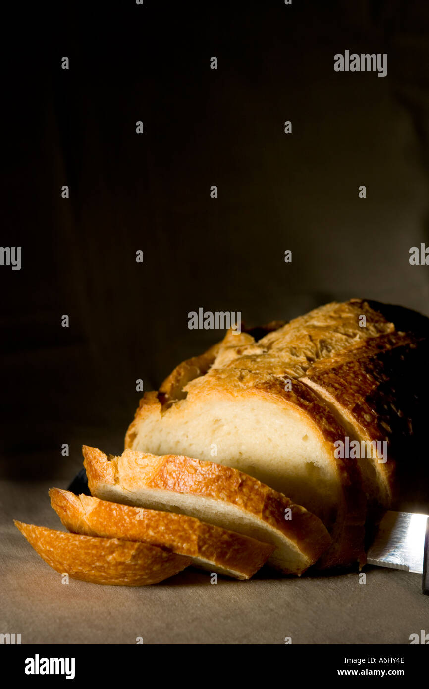Partially sliced fresh bread loaf on beige cloth with dark background ...