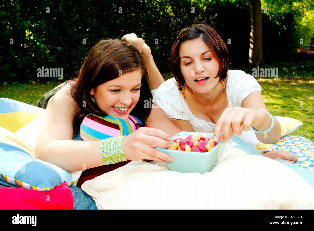 Young women lying on pillows in a garden eating fruit jellies Stock ...