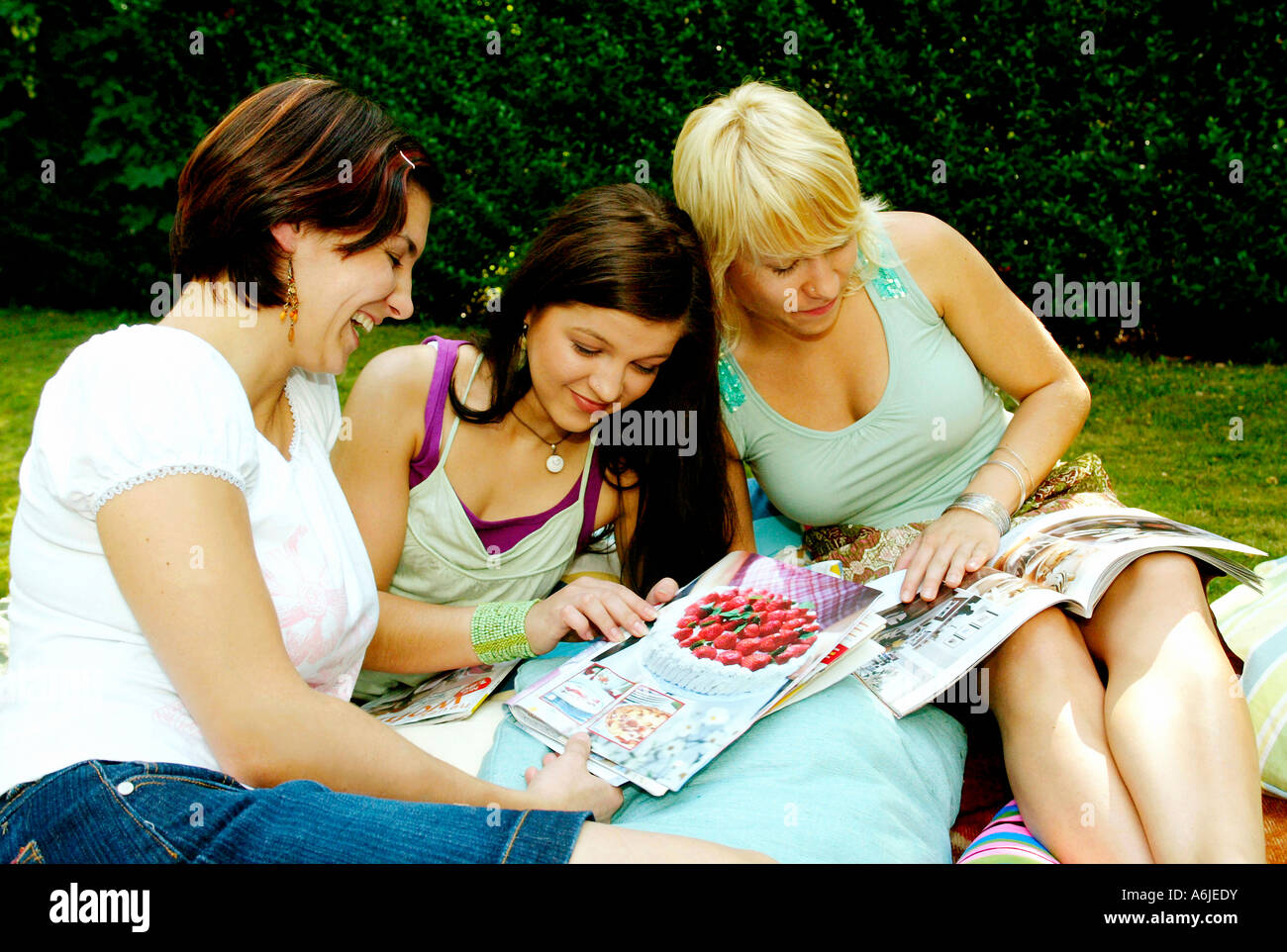 Young women in a garden reading magazines Stock Photo - Alamy
