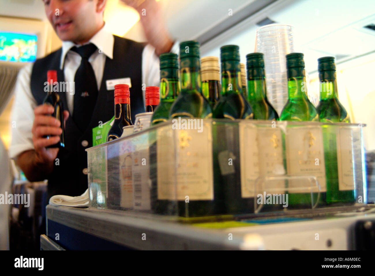 Male cabin crew steward serving wine and drinks from trolley on board ...