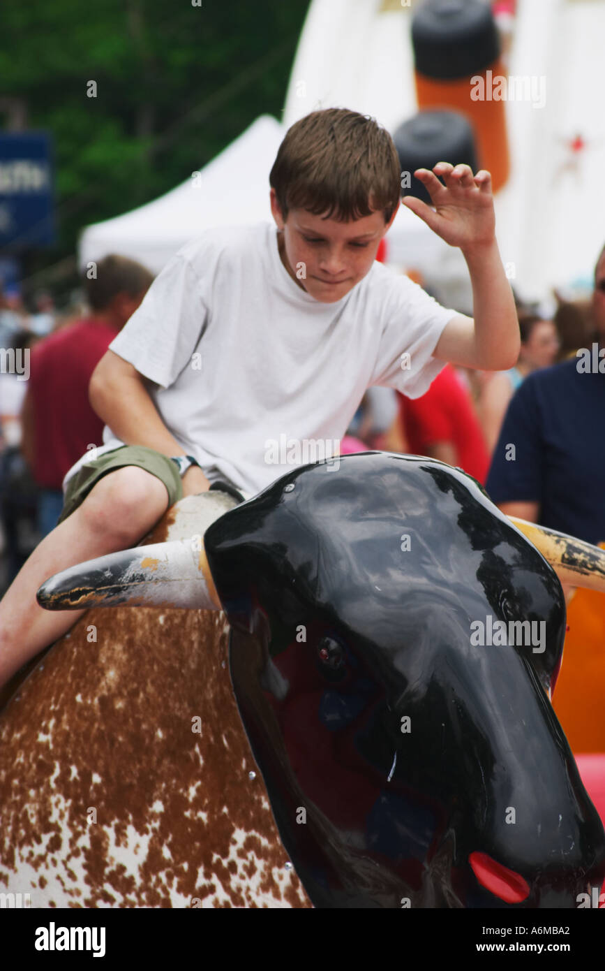 A young boy riding a mechanical bull at a local festival in East ...