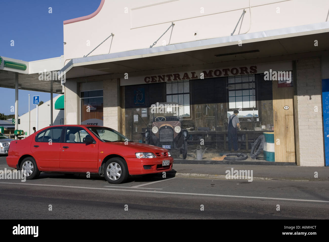 Red saloon car parked outside large mural depicting old Central Motors ...