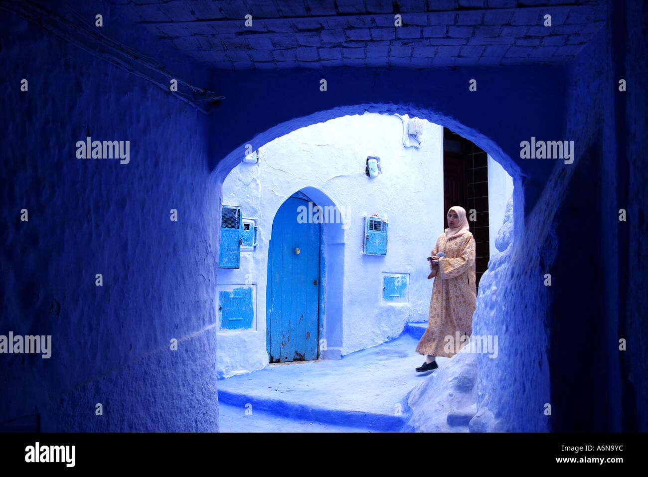 An Islam muslim woman burnoose jellaba robe walking through an arched ...