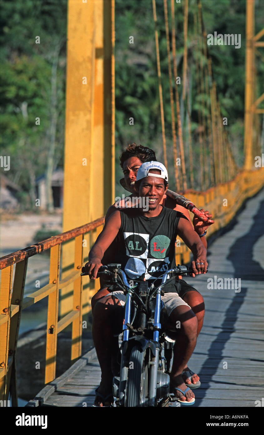 Young Balinese men travelling across a bridge by motorcycle Lembongan ...