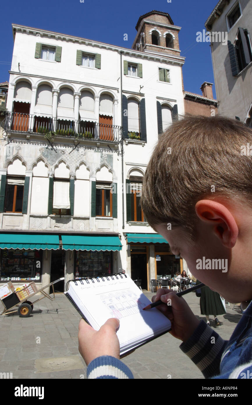 Young boy on holiday drawing a sketch of small square in Venice Italy ...