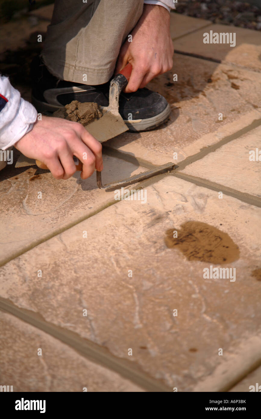 Close up of builder crouched pointing joints in paving of patio area ...