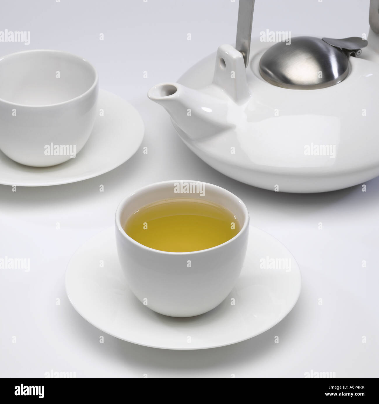 Empty tea cup and saucer sits with full cup of green tea and pot Stock ...