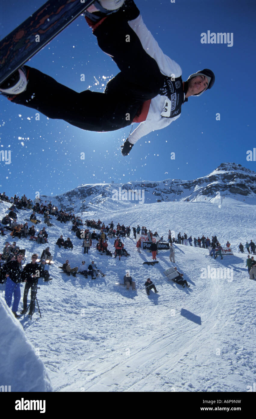 Competitive snowboarder in the pipe with a crowd of people looking on ...