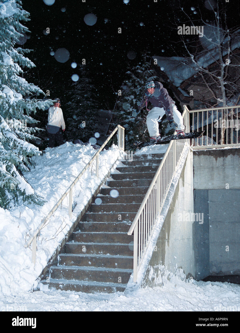 Snowboarder jibbing on a rail taken at the night with snow falling all ...