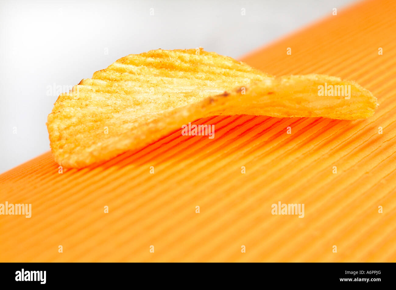 Flake of crisps on orange, stripped background Stock Photo - Alamy