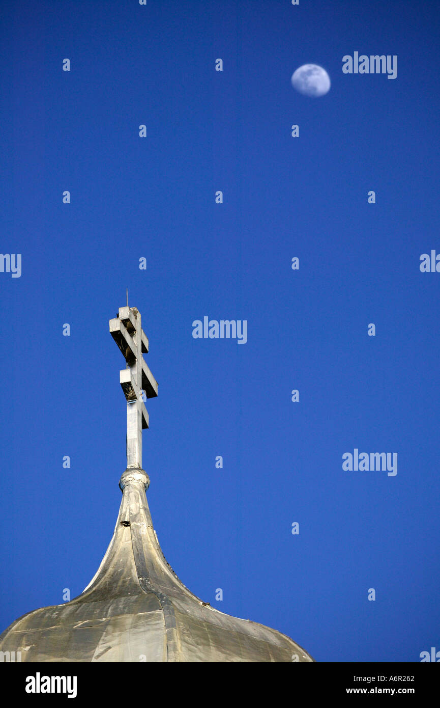 A half moon in the sky behind a dome of a church steeple and cross ...