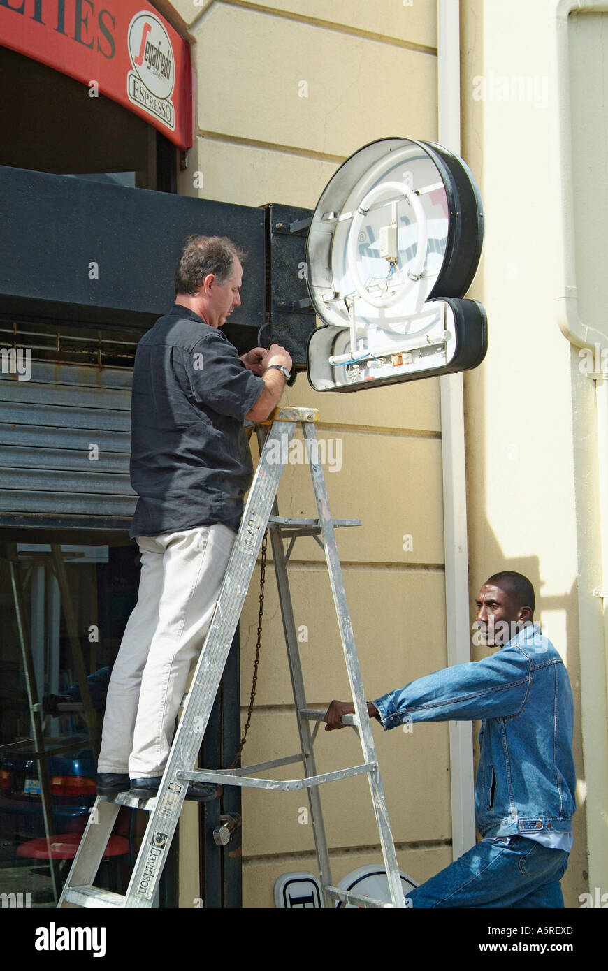 Man on ladder fixes sign Stock Photo - Alamy