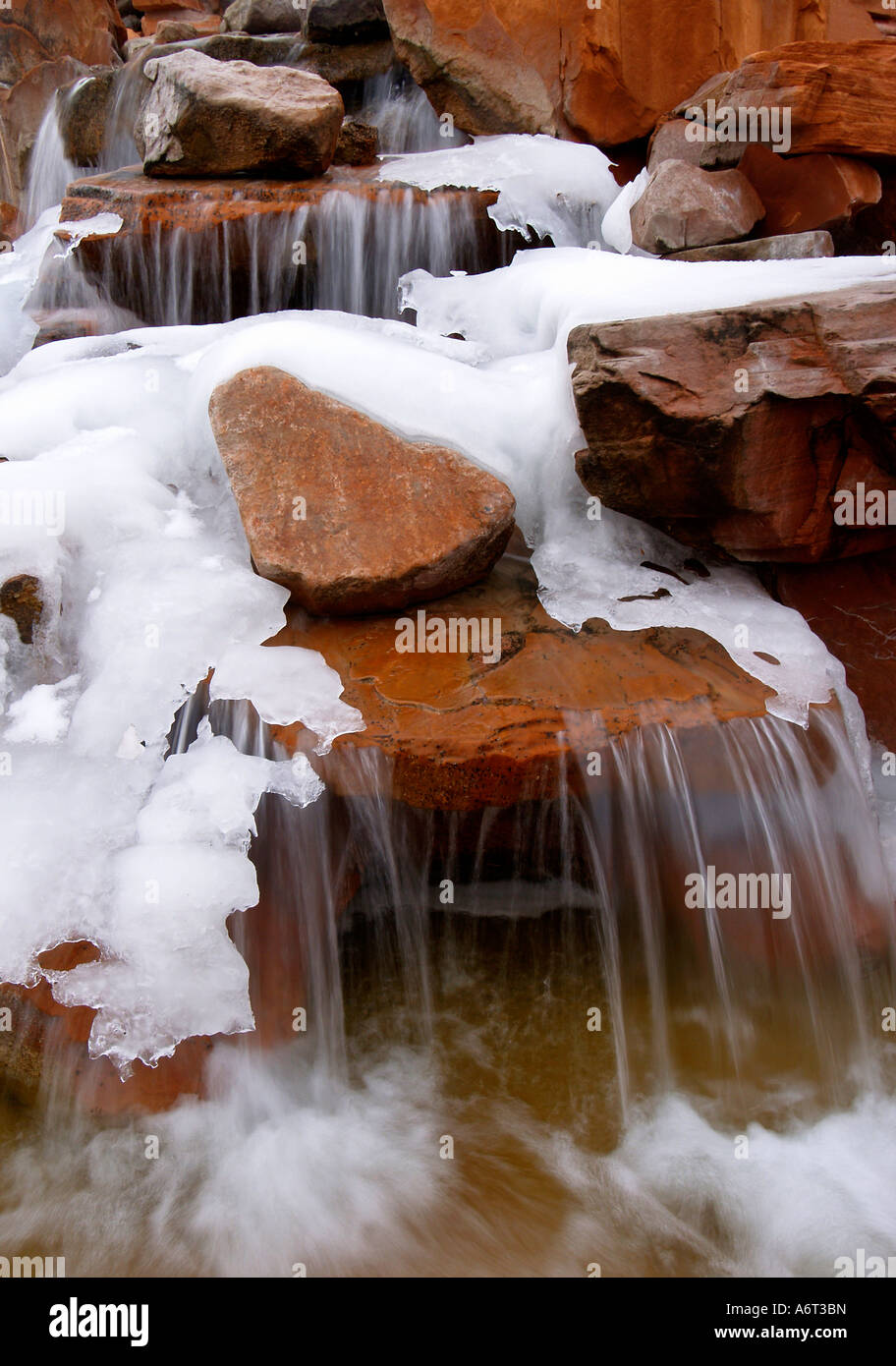 Icy water running beneath white snow, falling over red sandstone near ...