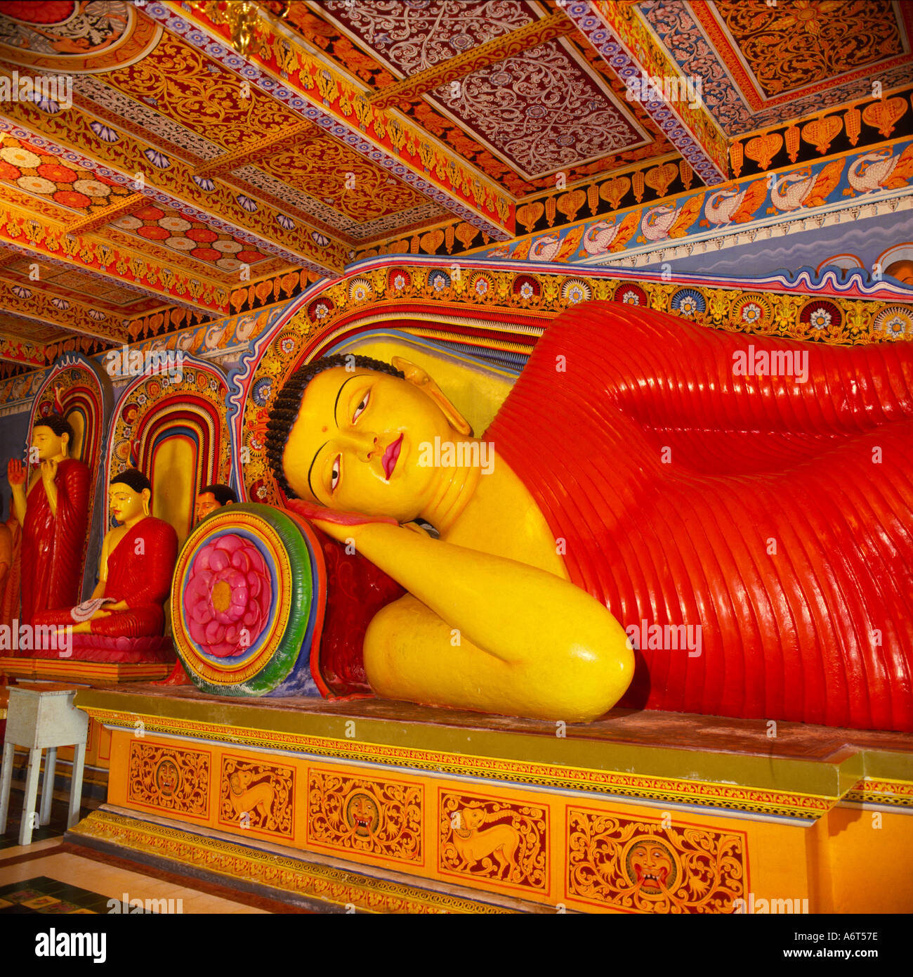 Brightly coloured red and yellow Buddha reclining with highly decorated ...