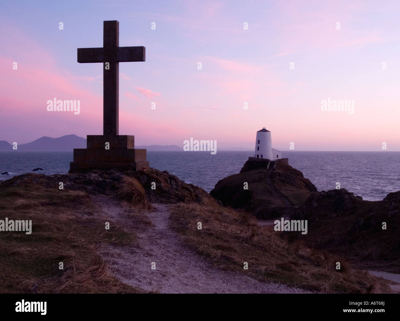 An ancient cross with a lighthouse as a backdrop on Llanddwyn Island in ...