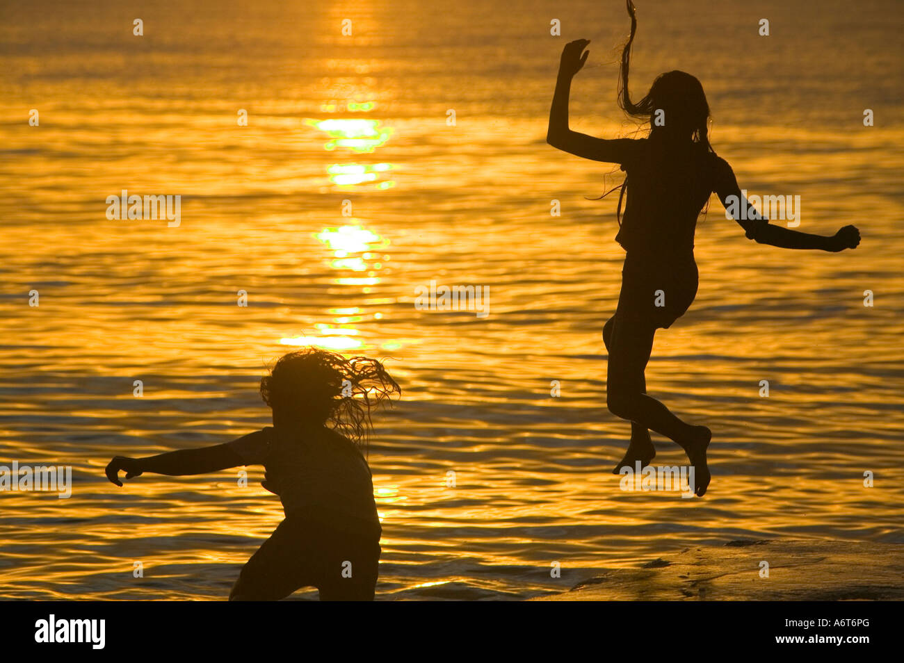Children leaping into the sea from a jetty on Funafuti island at sunset ...