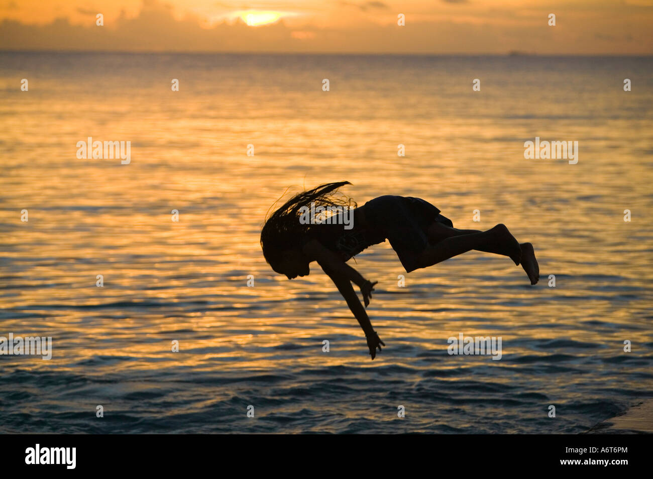 Children leaping into the sea from a jetty on Funafuti island at sunset ...