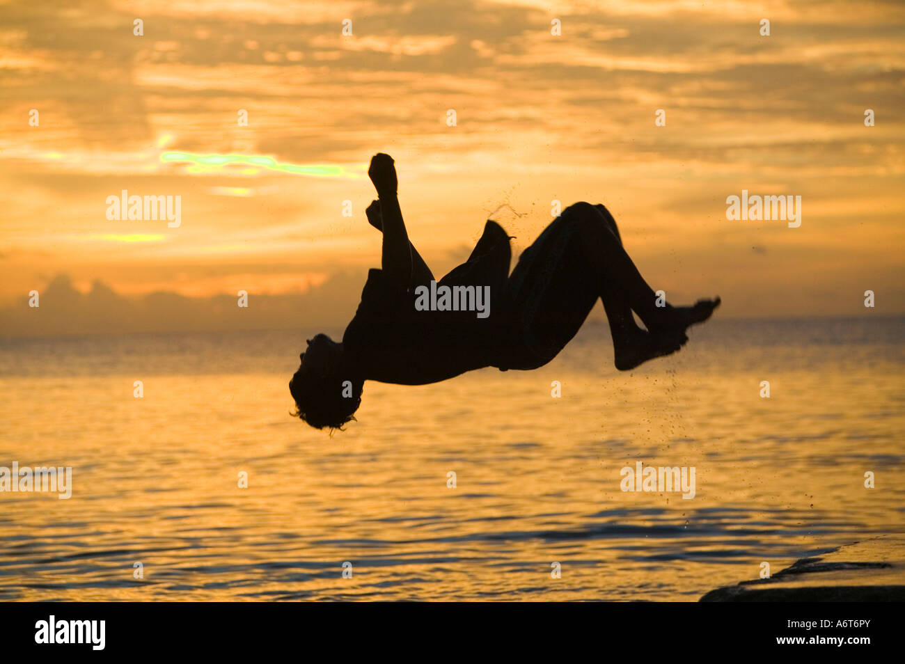 Children leaping into the sea from a jetty on Funafuti island at sunset ...