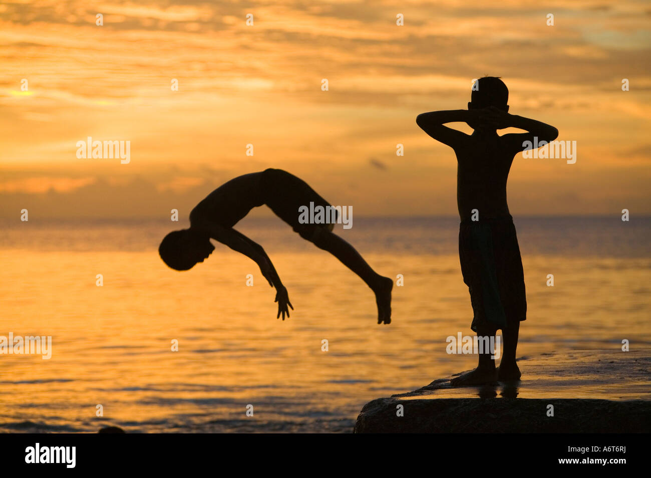Children leaping into the sea from a jetty on Funafuti island at sunset ...