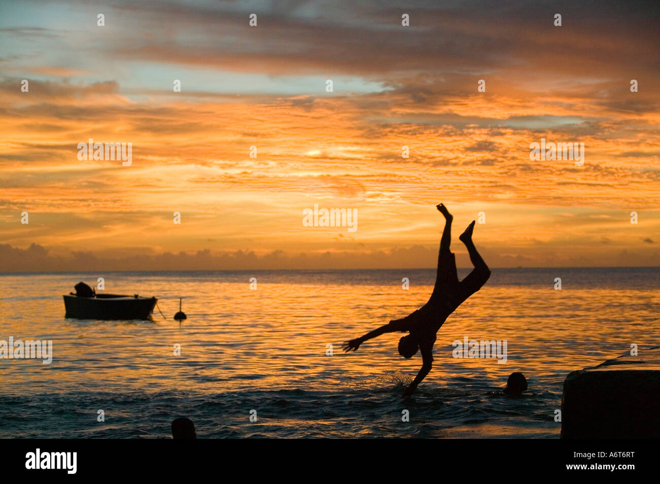 Children leaping into the sea from a jetty on Funafuti island at sunset ...