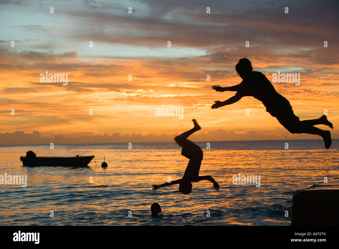 Children leaping into the sea from a jetty on Funafuti island at sunset ...