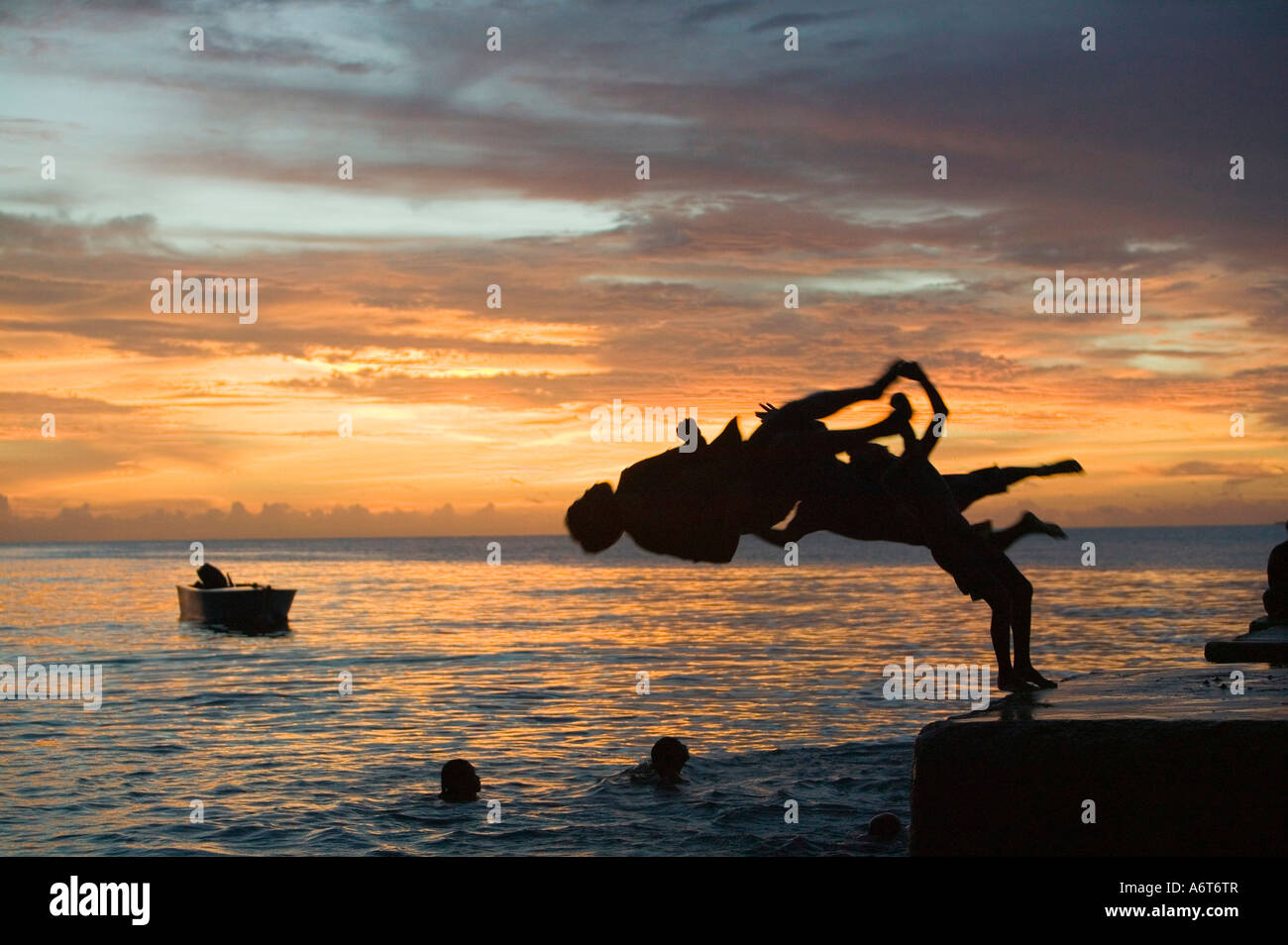 Children leaping into the sea from a jetty on Funafuti island at sunset ...